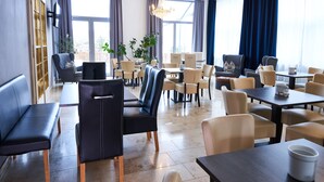 Um hall de hotel moderno com diversas opções de assento, incluindo sofás, cadeiras e mesas. Grandes janelas oferecem iluminação natural e vista para o exterior.