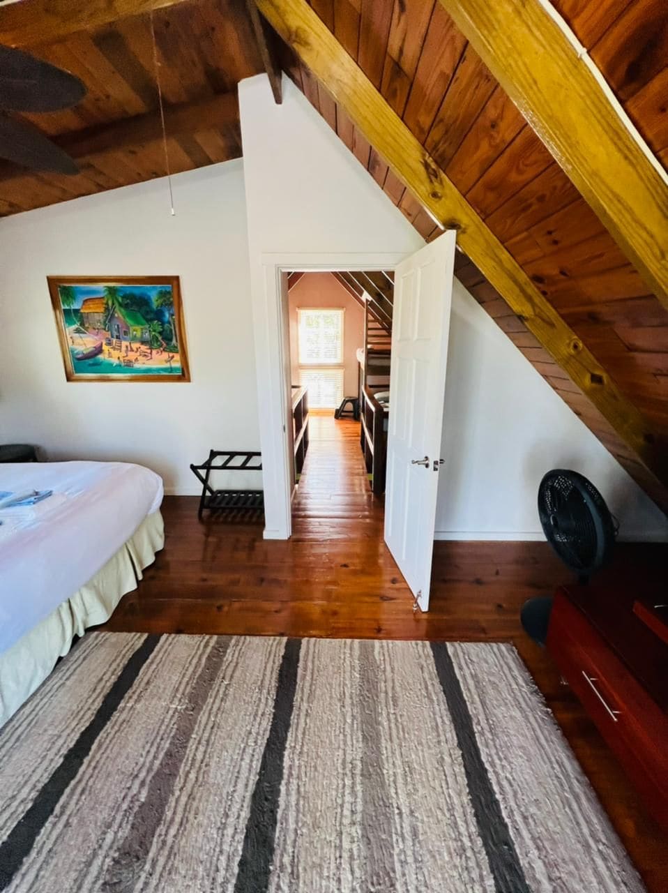 Quarto com cama, pintura, teto de madeira e vista para outro cômodo.