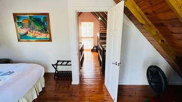 Quarto com cama, pintura, teto de madeira e vista para outro cômodo.