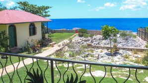 Um imóvel costeiro com um edifício de telhado vermelho, um jardim com diversas plantas e vista para o oceano.