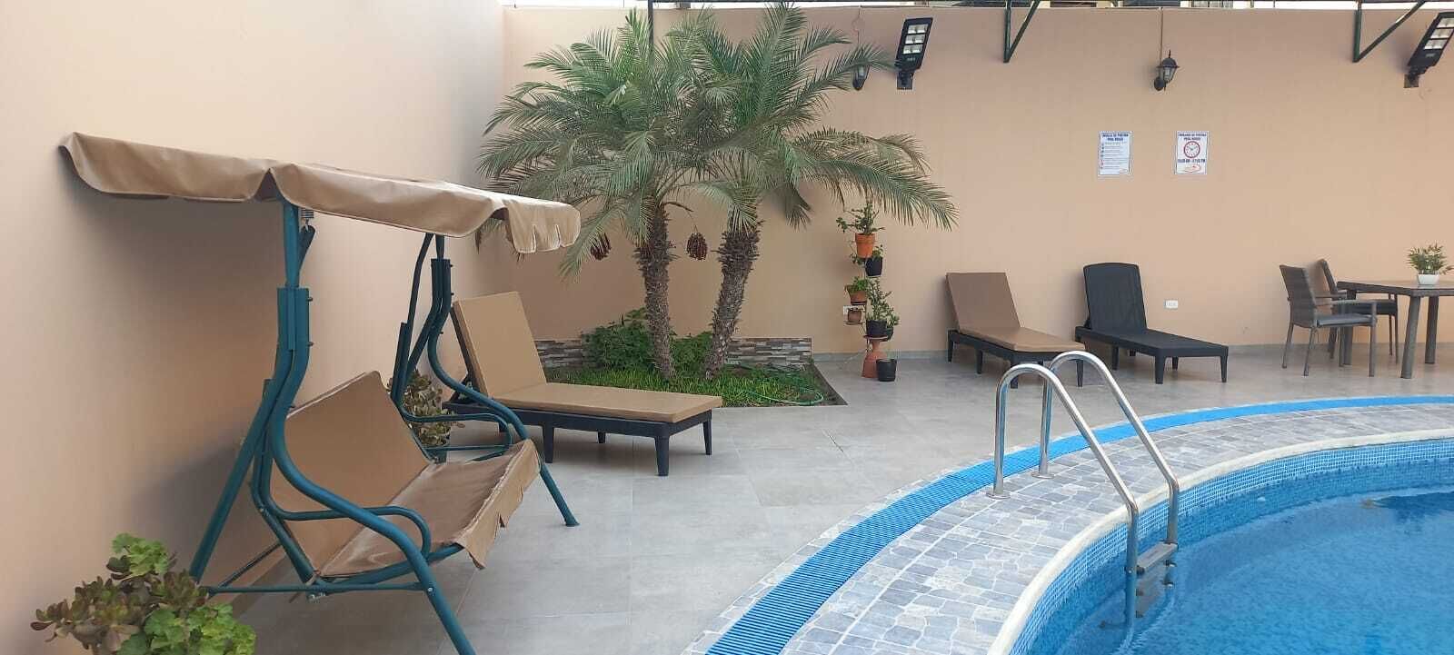 Uma área de piscina externa com espreguiçadeiras, um espaço coberto para relaxar e plantas em vasos.
