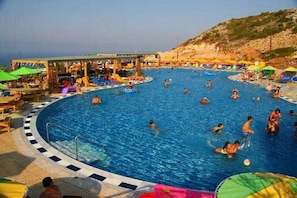 Uma grande piscina ao ar livre com várias pistas de natação, rodeada por espreguiçadeiras e guarda-sóis.