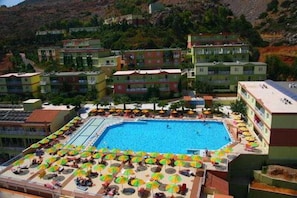 Um hotel com piscina central rodeada por espreguiçadeiras e guarda-sóis.