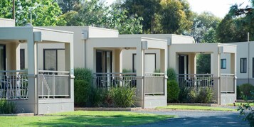 Uma fileira de casas móveis modernas, térreo, com varandas, em meio à vegetação.