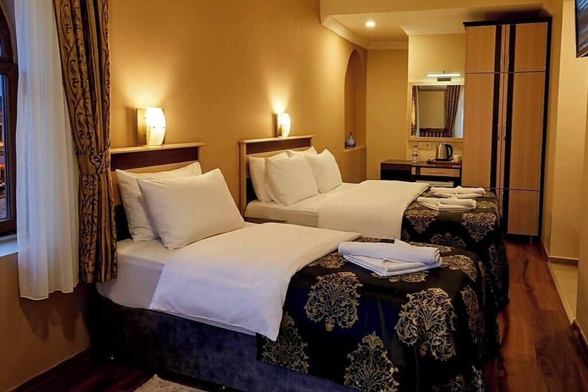 Quarto de hotel com duas camas, um espelho, um guarda-roupa e uma janela com cortinas.