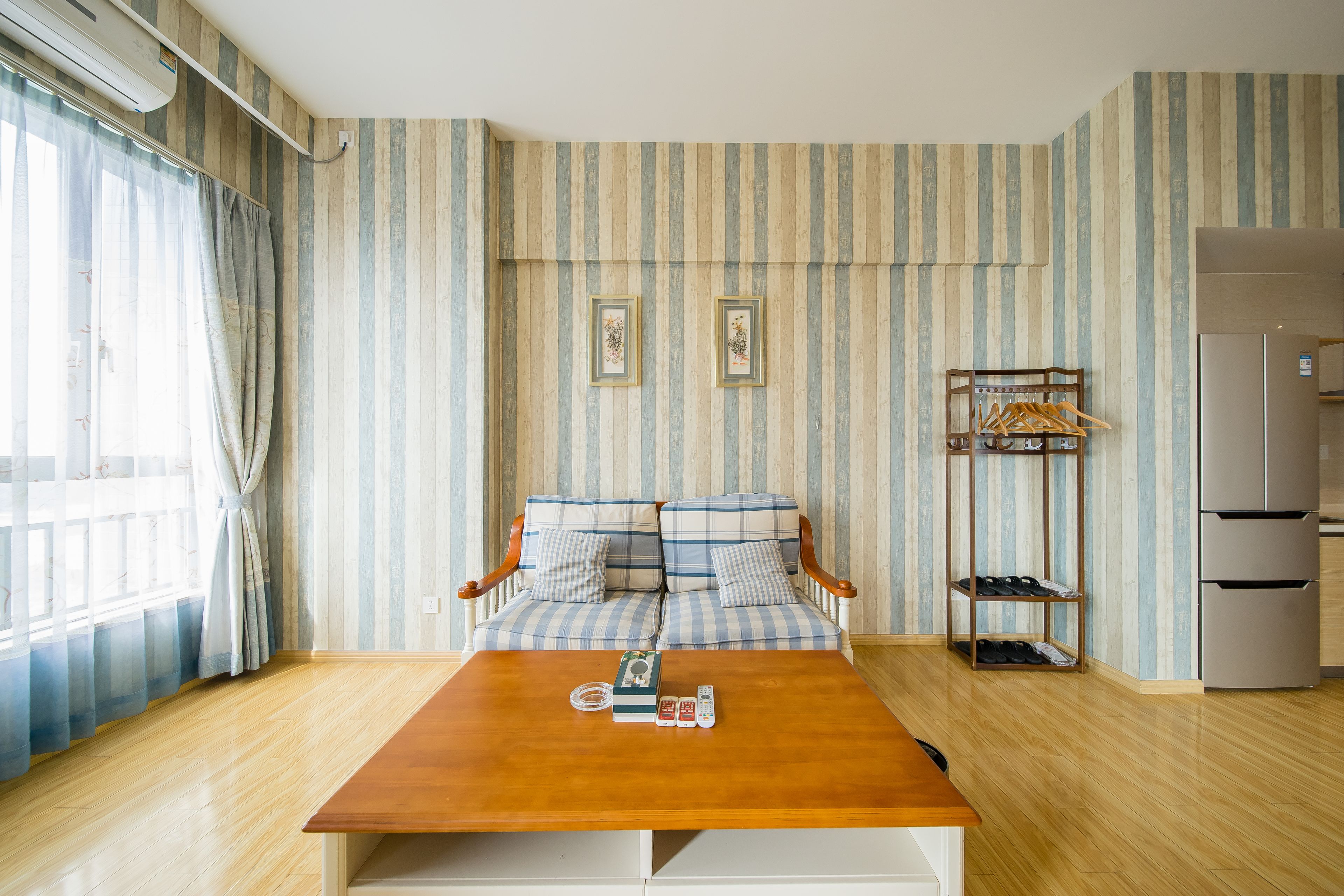 Quarto com mesa de madeira, sofá, papel de parede listrado e um sapateiro.