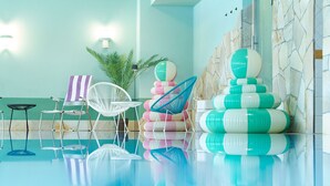 Uma área interna de piscina moderna, com piscina transparente, espreguiçadeiras e uma pilha decorativa de bolas de praia.