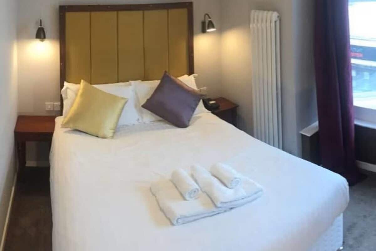 Quarto de hotel com uma cama grande, duas mesas de cabeceira, encosto de cama e uma janela com cortinas.