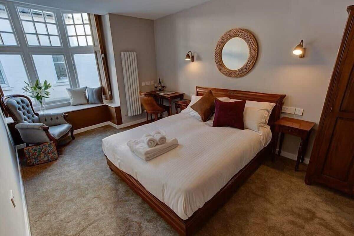 Quarto com cama grande, escrivaninha, cadeira e janela.