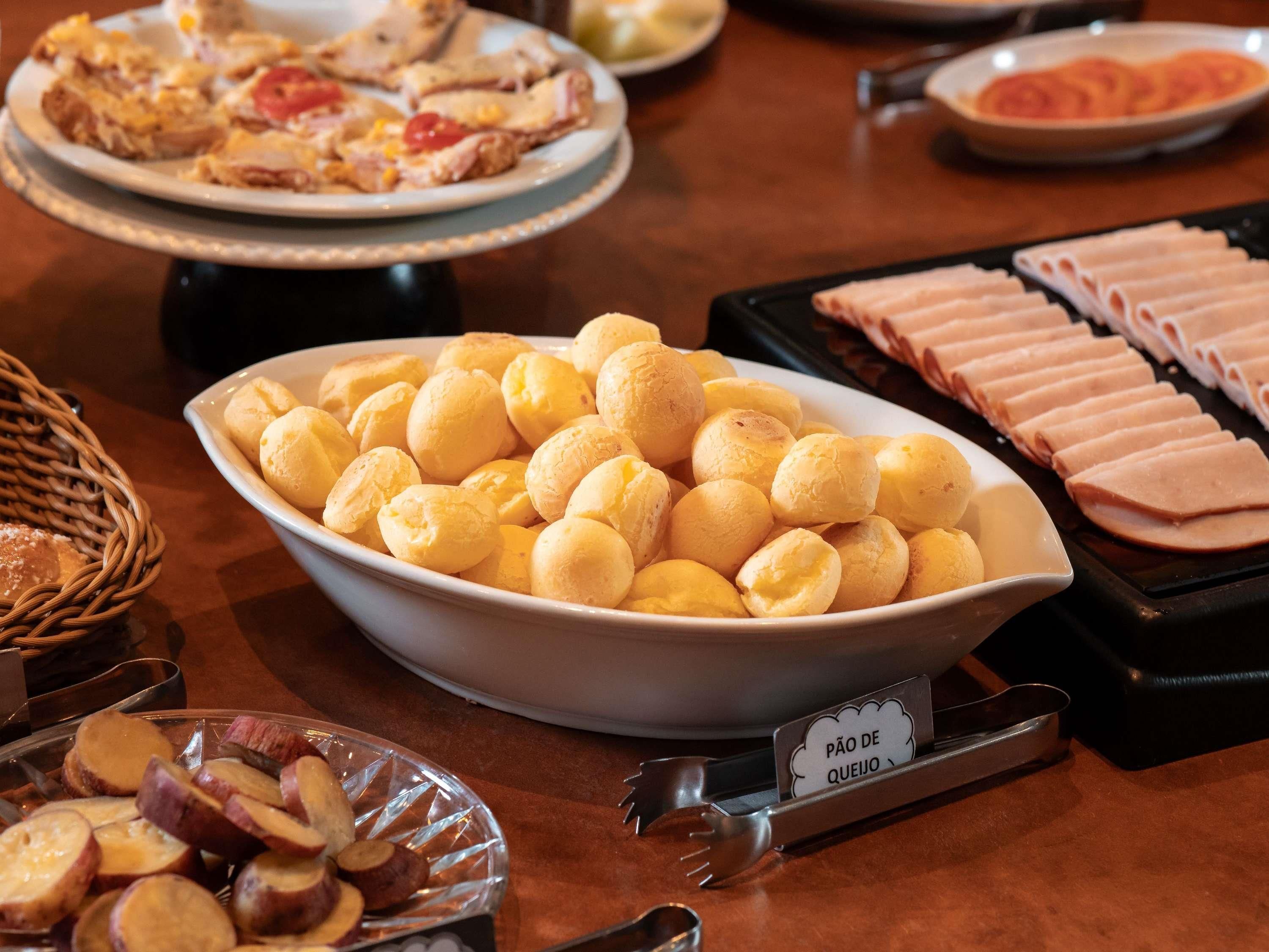 Buffet com diversos alimentos, incluindo uma tigela de bolinhas de queijo, presunto fatiado e um prato de legumes cortados.
