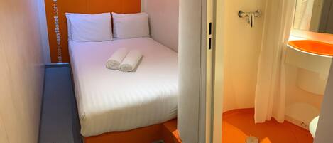 Quarto de hotel com cama e banheiro com chão laranja e pia branca.
