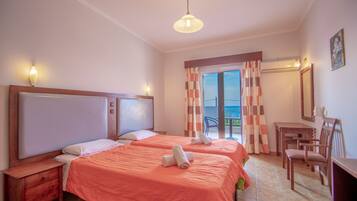 Quarto de hotel com duas camas, uma escrivaninha, uma cadeira e uma varanda com vista.