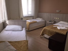 Quarto de hotel com duas camas de solteiro, uma cama de casal, uma mesa de cabeceira com telefone e um pequeno banquinho preto.