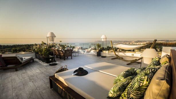 Terraço no telhado com um sofá, cadeiras e uma rede, com vista para a paisagem urbana.