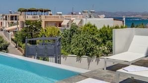 Uma área de piscina no terraço com espreguiçadeiras e piscina, com vista para uma área residencial com edifícios e um céu azul límpido.