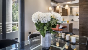 Cozinha moderna com armários de madeira, sala de jantar com mesa de vidro e um vaso com flores brancas.