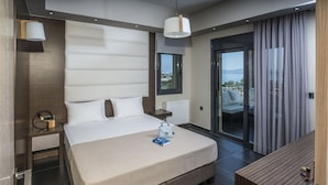 Quarto de hotel moderno com uma cama grande, uma mesa de cabeceira, uma escrivaninha de madeira e vista para o exterior por uma porta de correr de vidro.