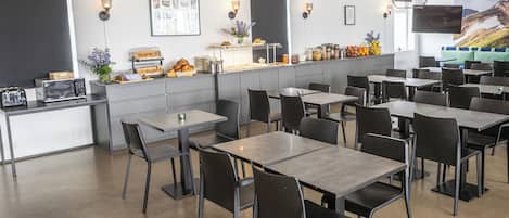 Um restaurante moderno com balcão, mesas, cadeiras e uma televisão de tela plana.