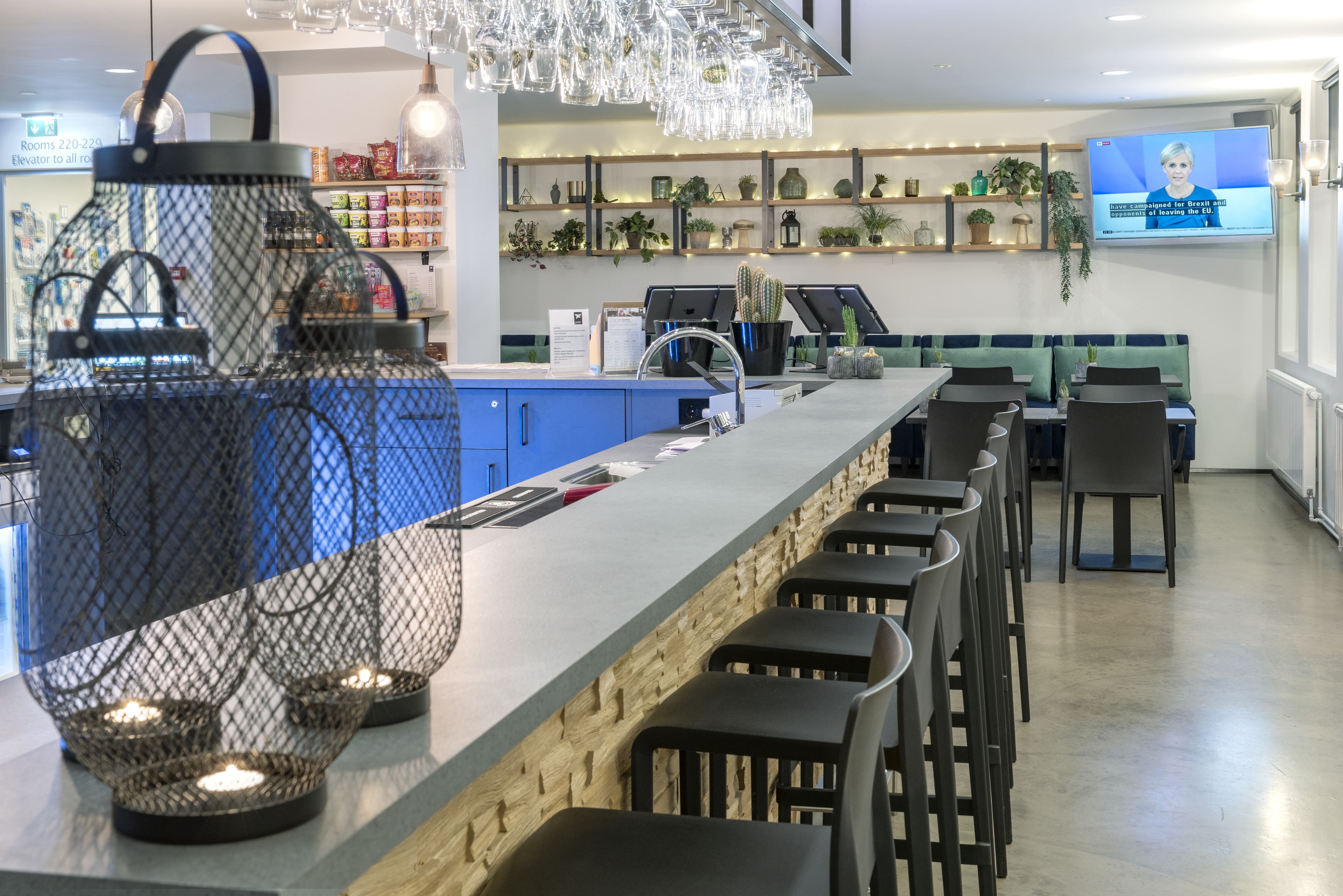 Uma área de bar moderna com um balcão comprido, banquetas e uma televisão exibindo uma transmissão de notícias.