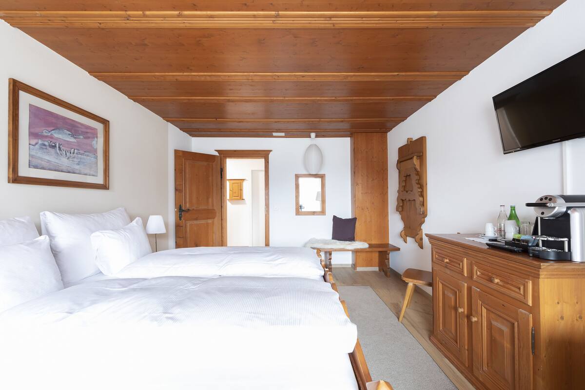 Quarto de hotel com duas camas, teto de madeira, televisão e armário de madeira.