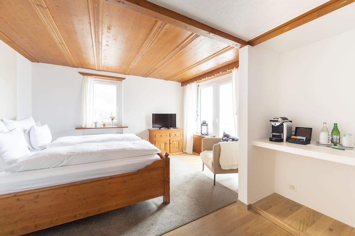 Quarto com cama de madeira, televisão, escrivaninha e prateleira com garrafas.