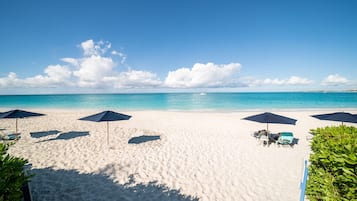 Na praia, areia branca, espreguiçadeiras, guarda-sóis