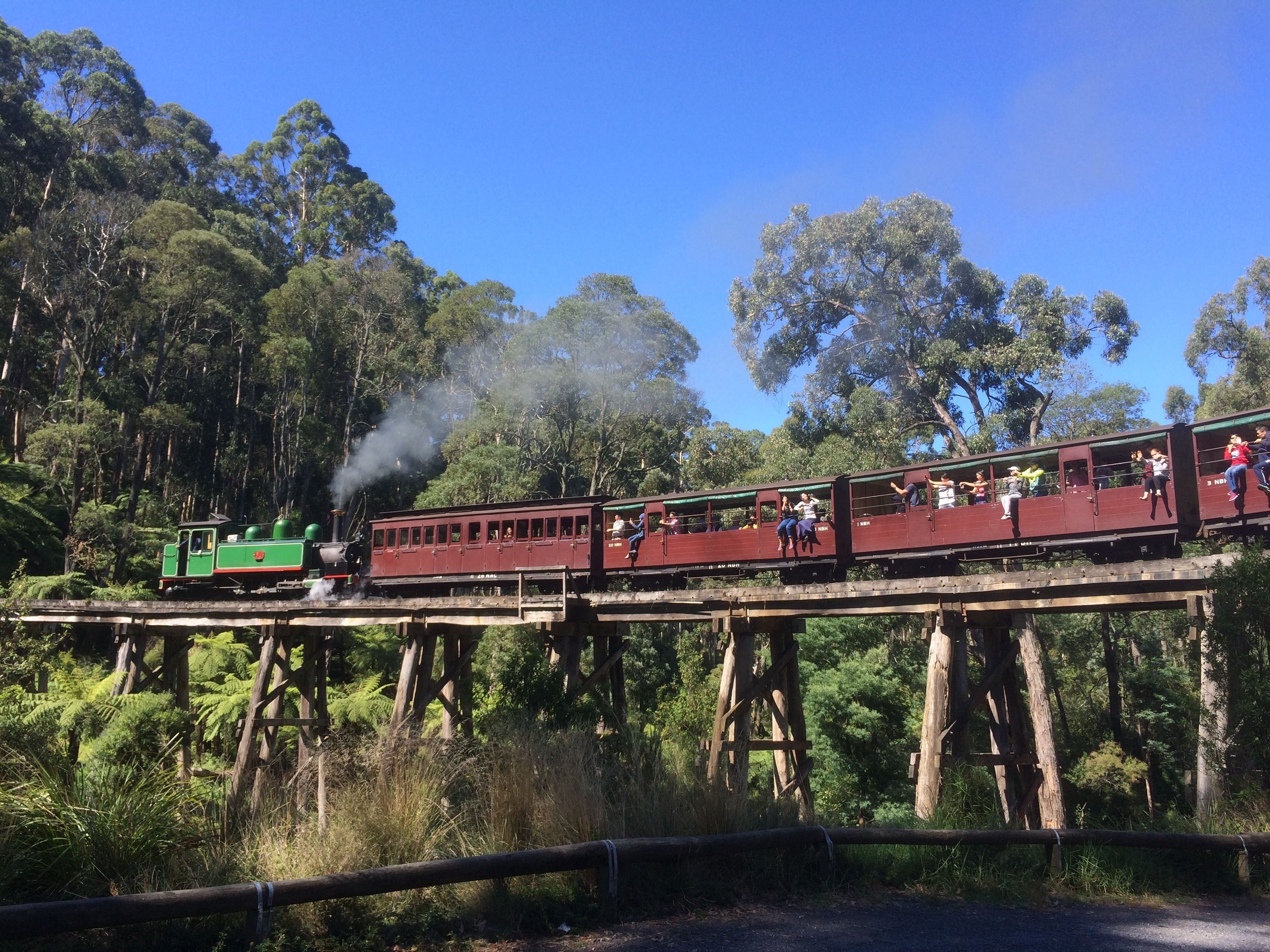 Um trem a vapor sobre uma ponte de madeira, com passageiros.