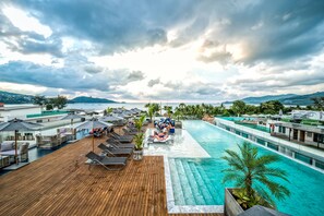 Uma área de piscina no terraço com espreguiçadeiras, guarda-sóis e vista para o mar e montanhas.