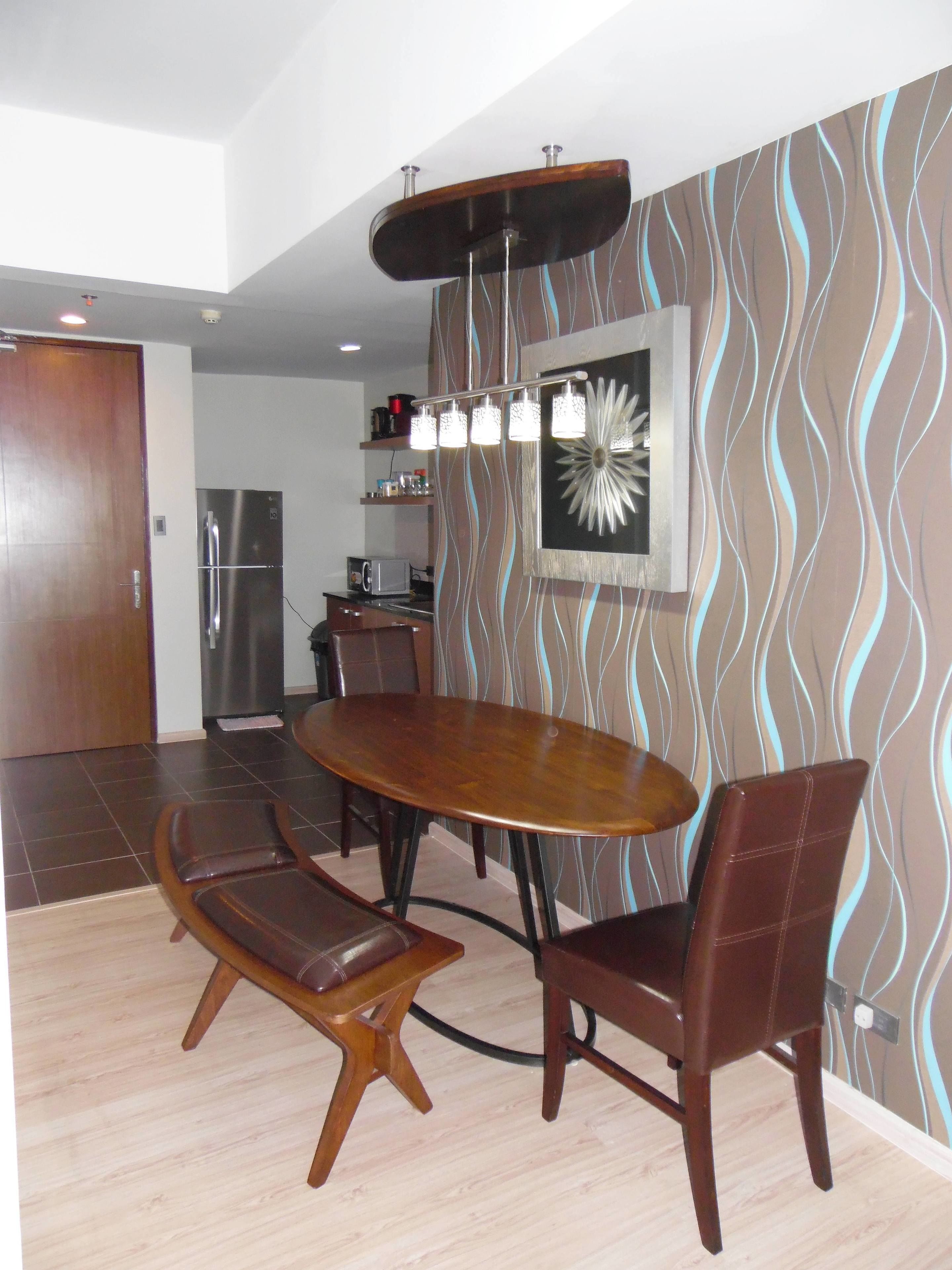 Uma sala de jantar com uma mesa de madeira e quatro cadeiras, geladeira, micro-ondas e um objeto decorativo na parede.