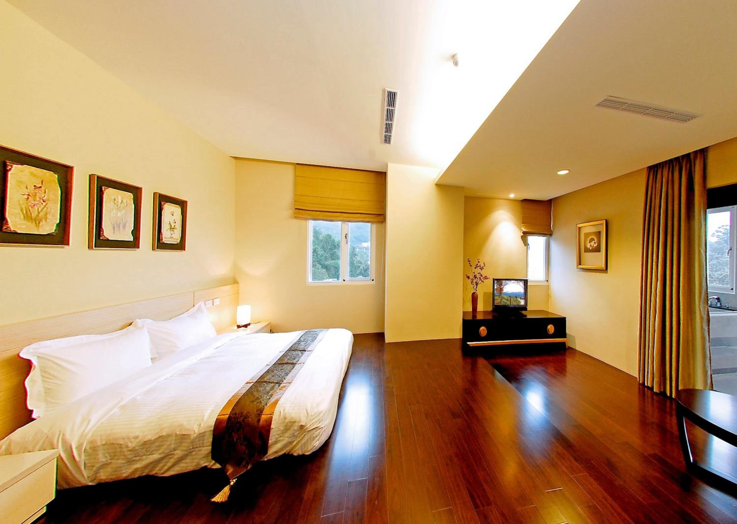 Quarto de hotel espaçoso com uma cama grande, uma escrivaninha, televisão e obras de arte emolduradas nas paredes.