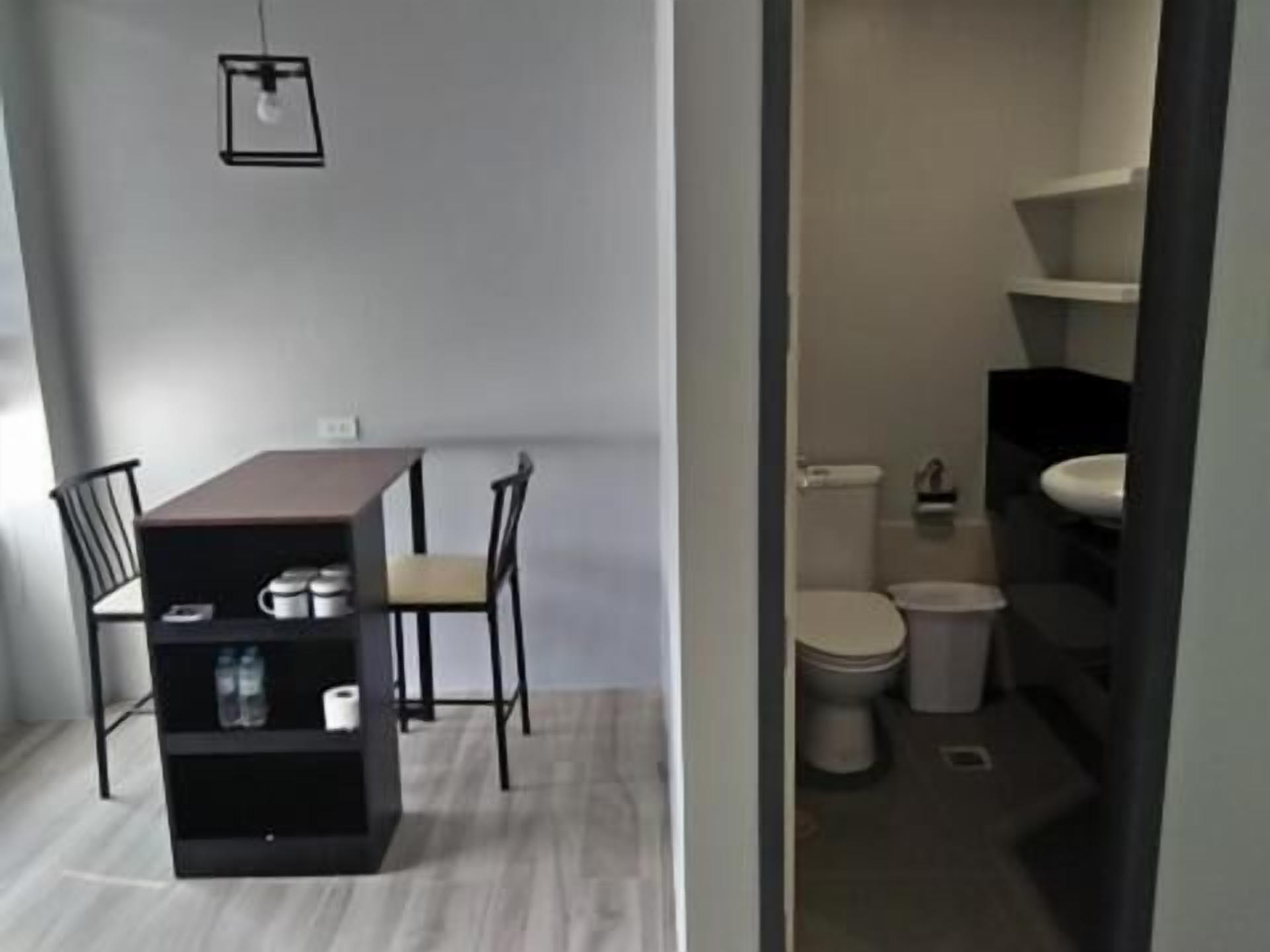 Quarto pequeno e moderno, com uma mesa e cadeiras de madeira, uma unidade de armazenamento preta e um luminário simples.