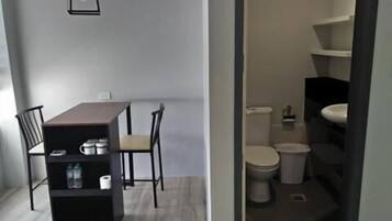 Quarto pequeno e moderno, com uma mesa e cadeiras de madeira, uma unidade de armazenamento preta e um luminário simples.