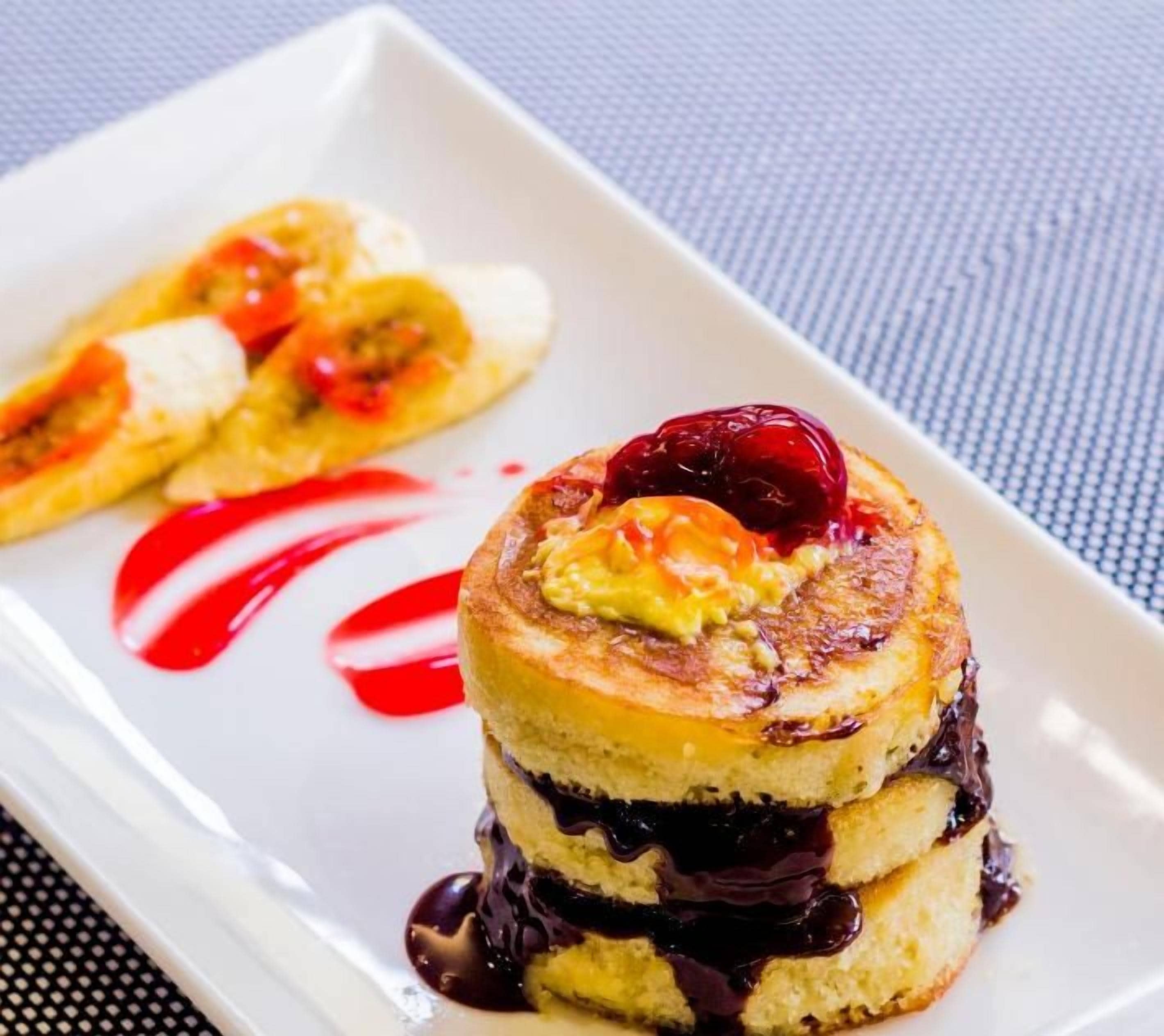 Pequenos panquecas fofinhos com molho de frutas vermelhas sobre um prato branco.