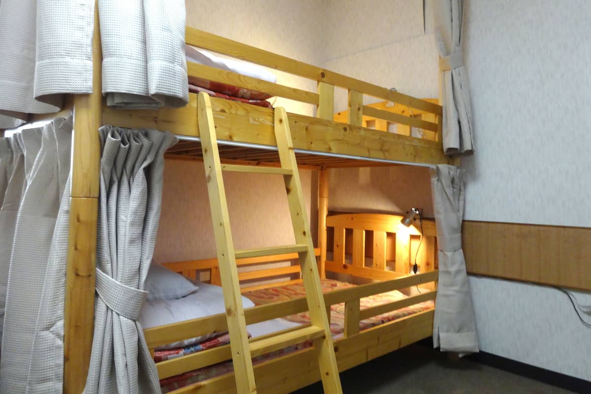 Quarto com beliche, uma escada de madeira, uma cama de solteiro com travesseiro e uma cortina.