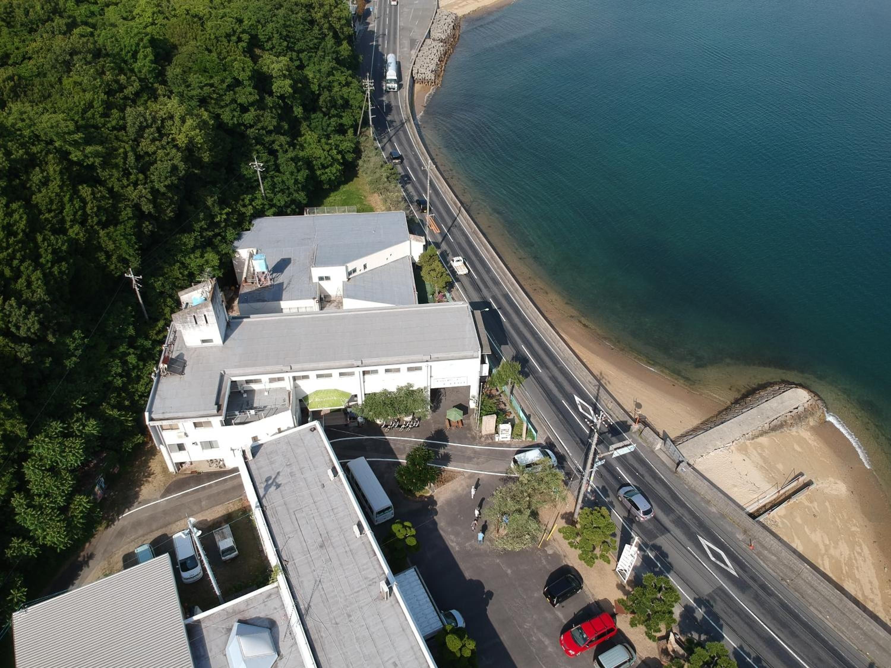 Vista aérea de uma propriedade costeira com uma estrada que leva a uma praia, cercada por vegetação densa.
