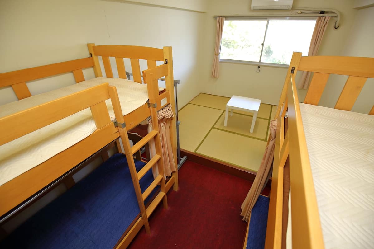 Quarto com beliches, uma mesa pequena e uma janela com cortinas.