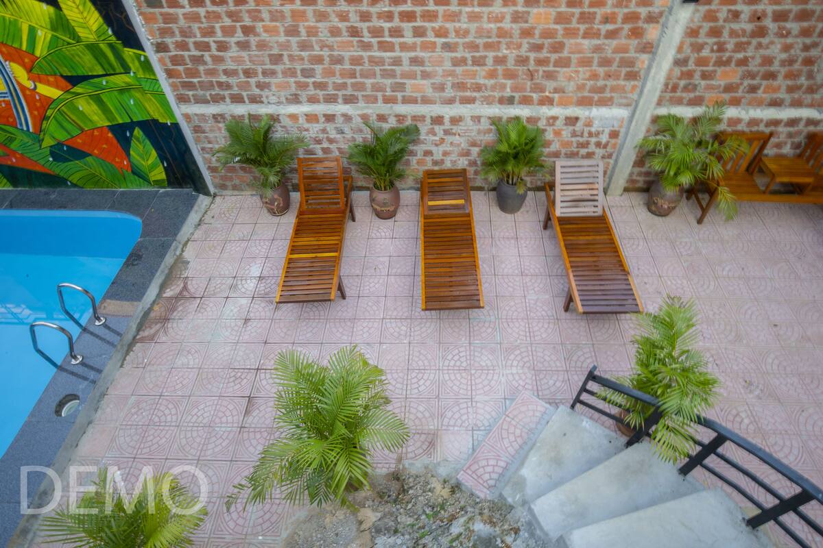 Terraço no telhado com piscina, cadeiras de descanso, plantas em vasos e uma parede de tijolos.
