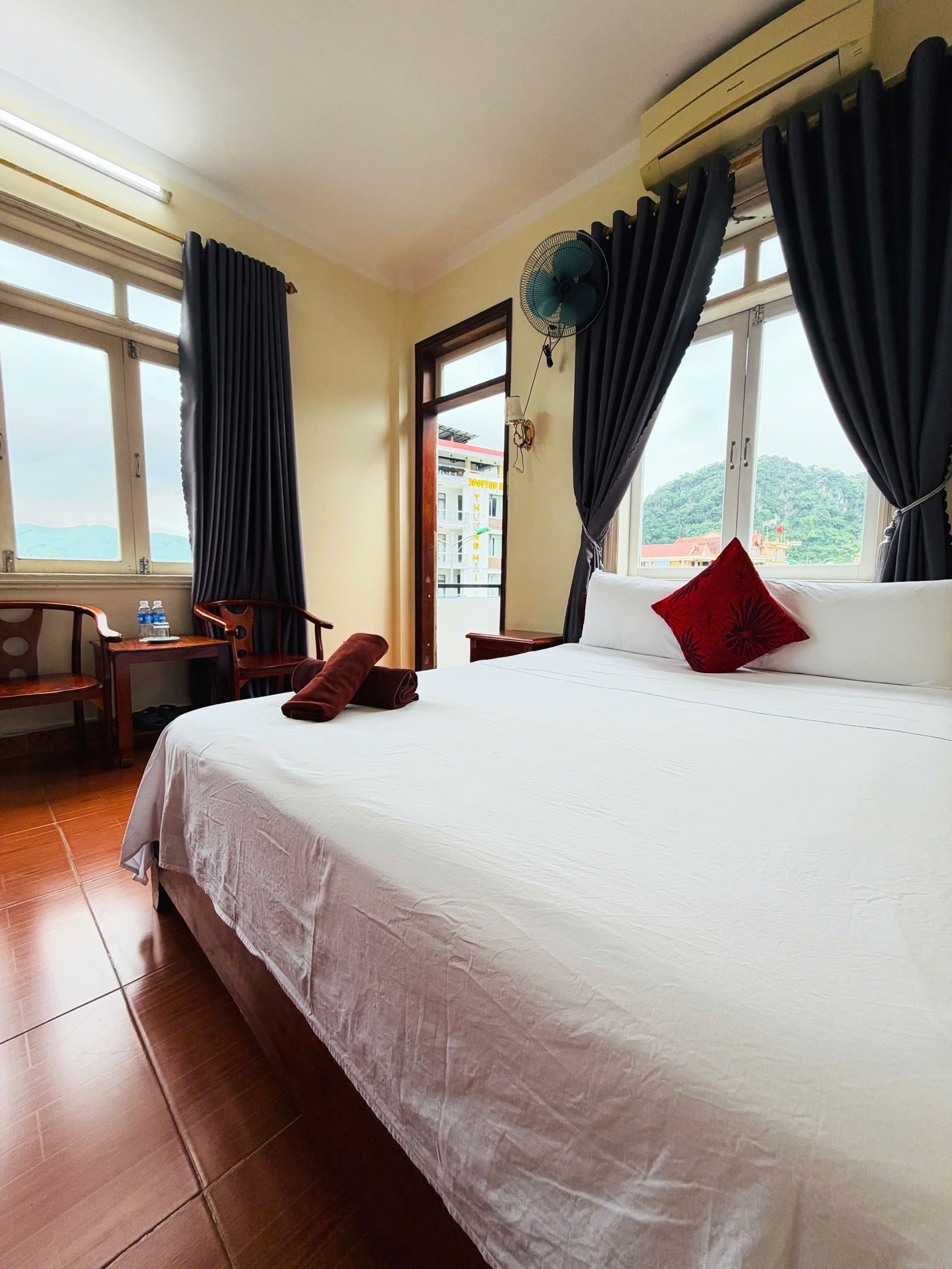 Quarto de hotel com cama, escrivaninha, cadeira, janela com cortinas e ar condicionado.