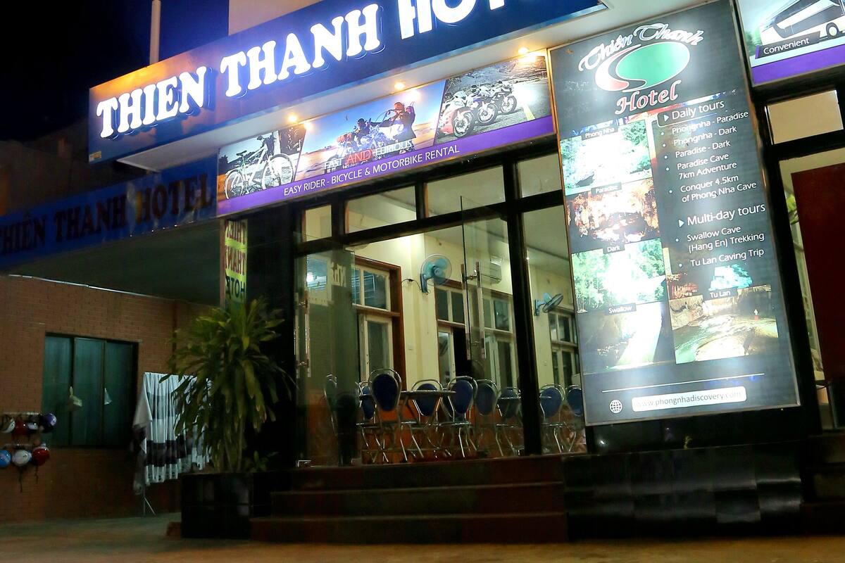 Um hotel com uma placa grande que diz "THIEN THANH HOTEL" e um painel exibindo passeios e atividades.
