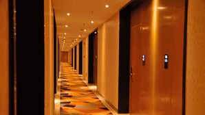 Corredor de hotel com carpete estampado, portas de madeira e um longo hall.