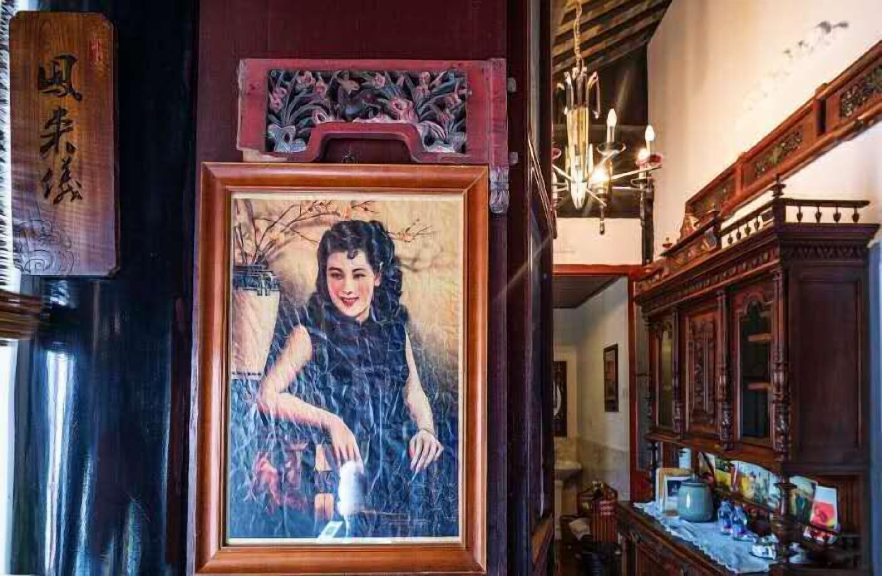Um retrato emoldurado com um painel de madeira decorativo acima, um candelabro e um armário de madeira com diversos objetos em cima.