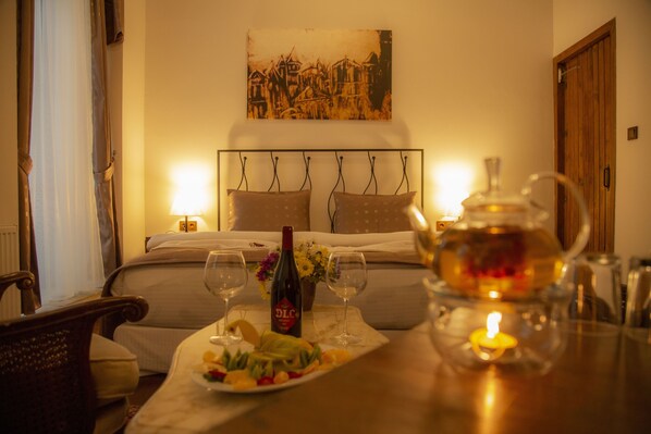 Quarto de hotel com cama, mesa de cabeceira, garrafa de vinho, copos e uma vela.
