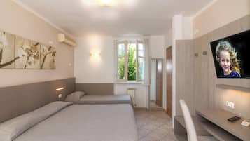 Quarto de hotel com duas camas, televisão, janela com cortinas e radiador.