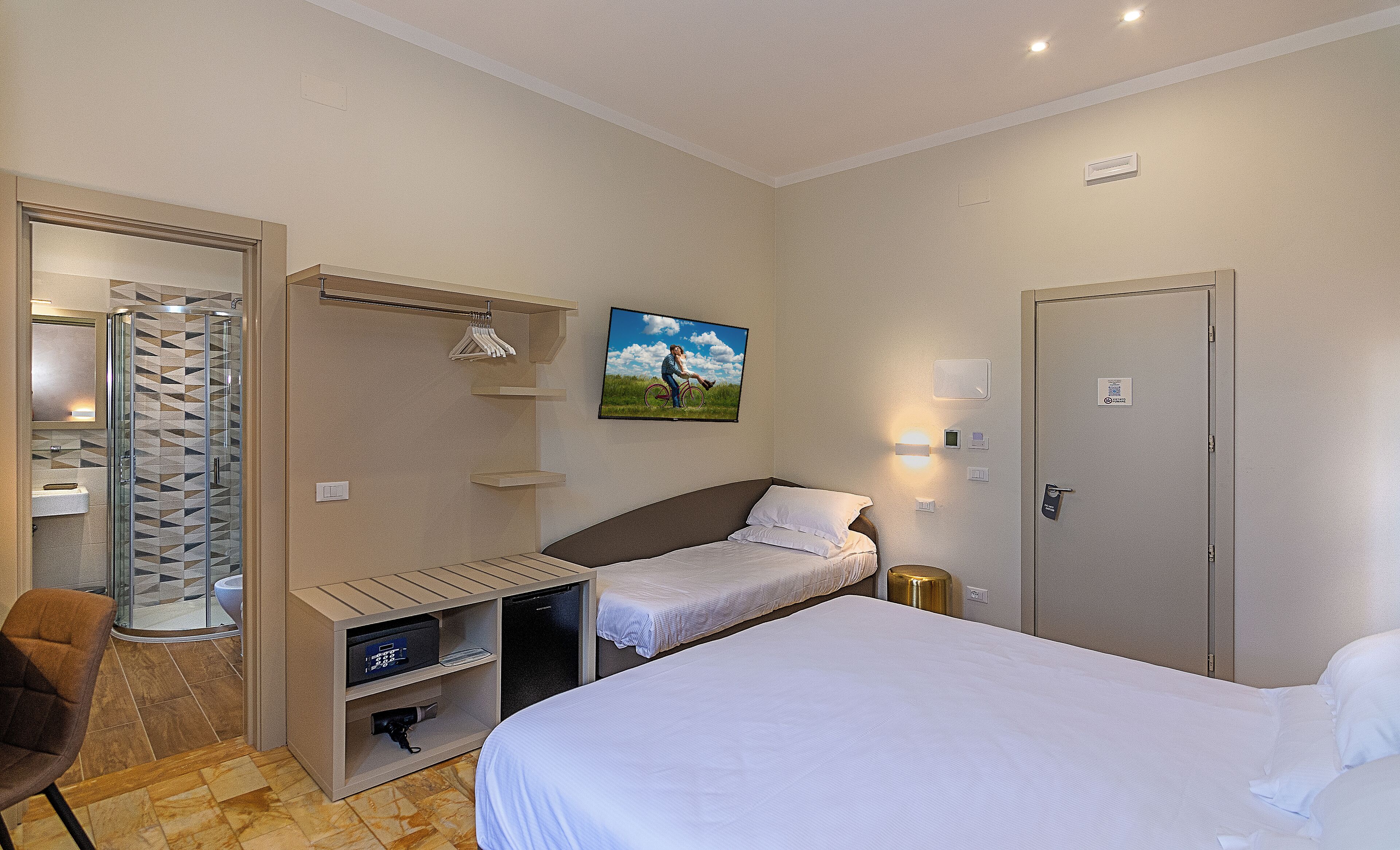 Quarto de hotel com cama, escrivaninha, cadeira, chuveiro e televisão.