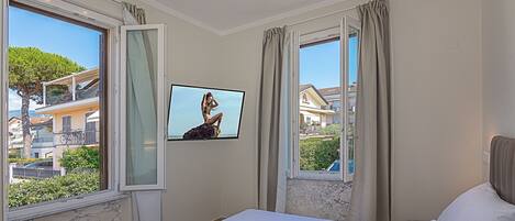 Quarto com uma cama, televisão na parede e vista para uma área residencial.