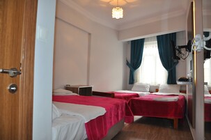 Quarto de hotel com duas camas de solteiro, porta de madeira, uma mesinha e janela com cortinas.