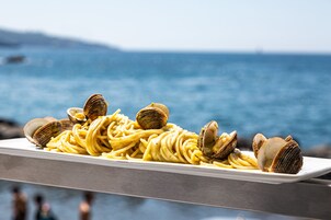 Prato de massa com amêijoas sobre um corrimão, com vista para o mar.