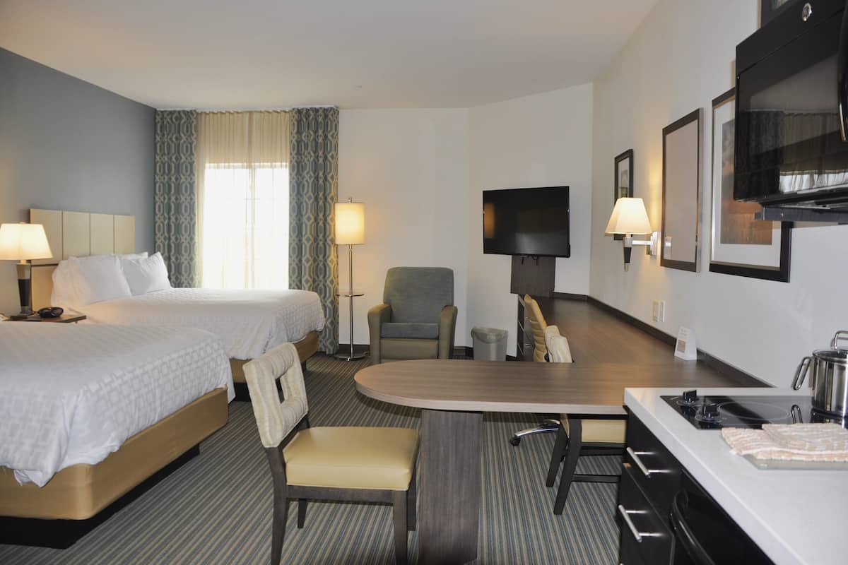 Quarto de hotel com duas camas, uma mesa de jantar, televisão e um pequeno espaço de estar.