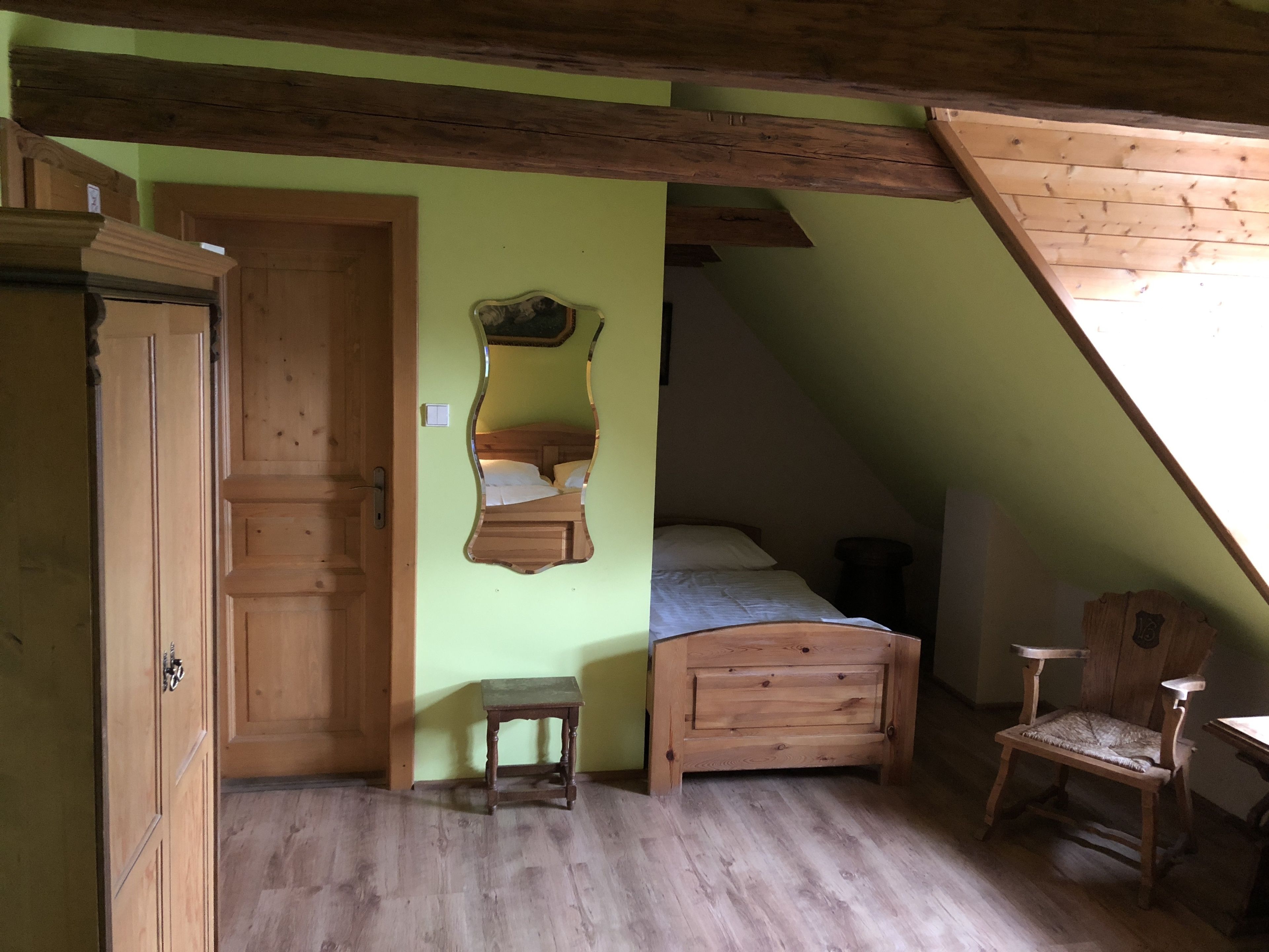 Quarto com teto inclinado, uma cama de madeira, uma pequena mesa de madeira, uma cadeira e um guarda-roupa.