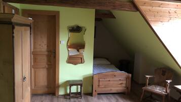 Quarto com teto inclinado, uma cama de madeira, uma pequena mesa de madeira, uma cadeira e um guarda-roupa.
